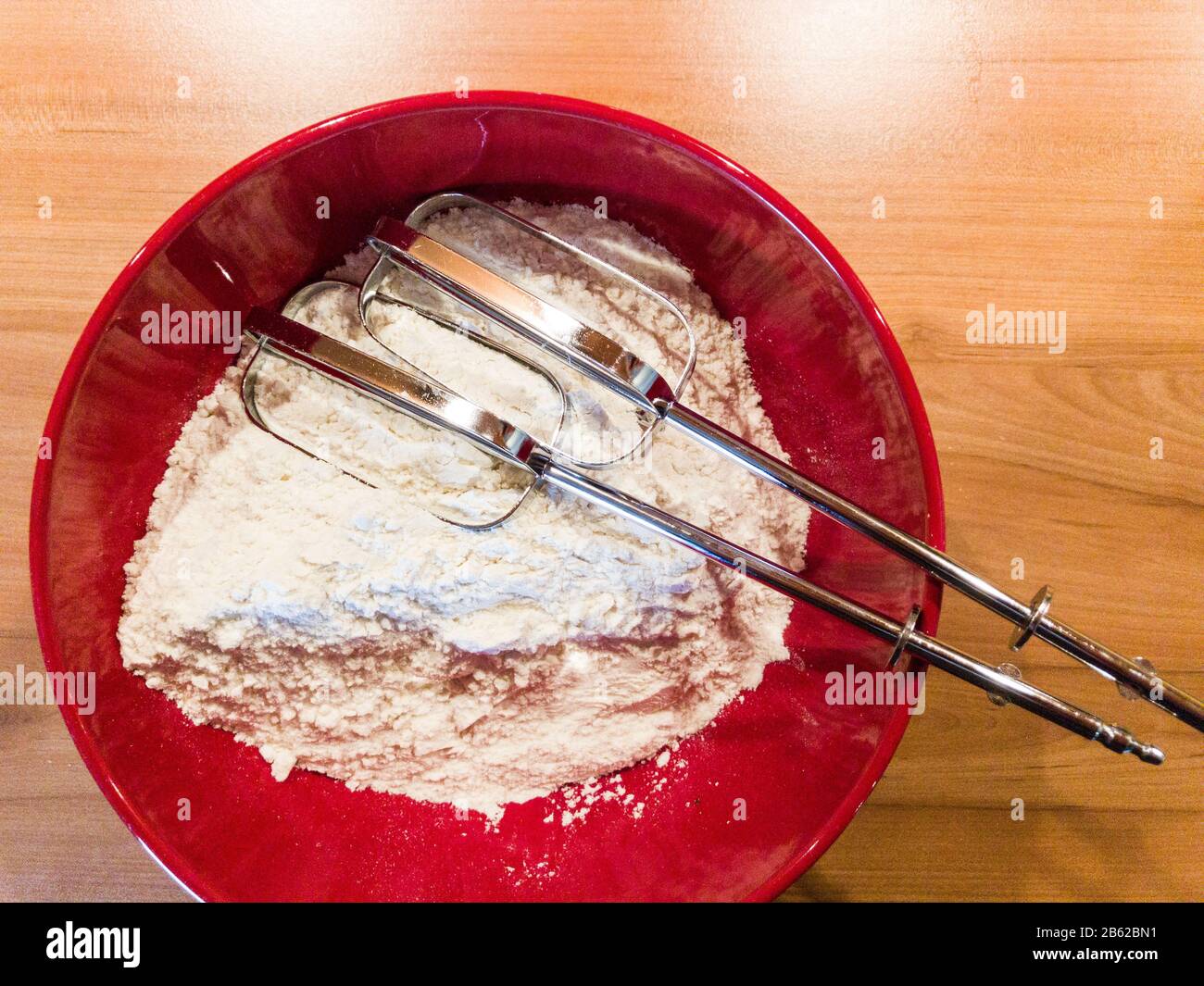 Dry flour in a red bowl with mixing sticks on wooden kitchen desk ...