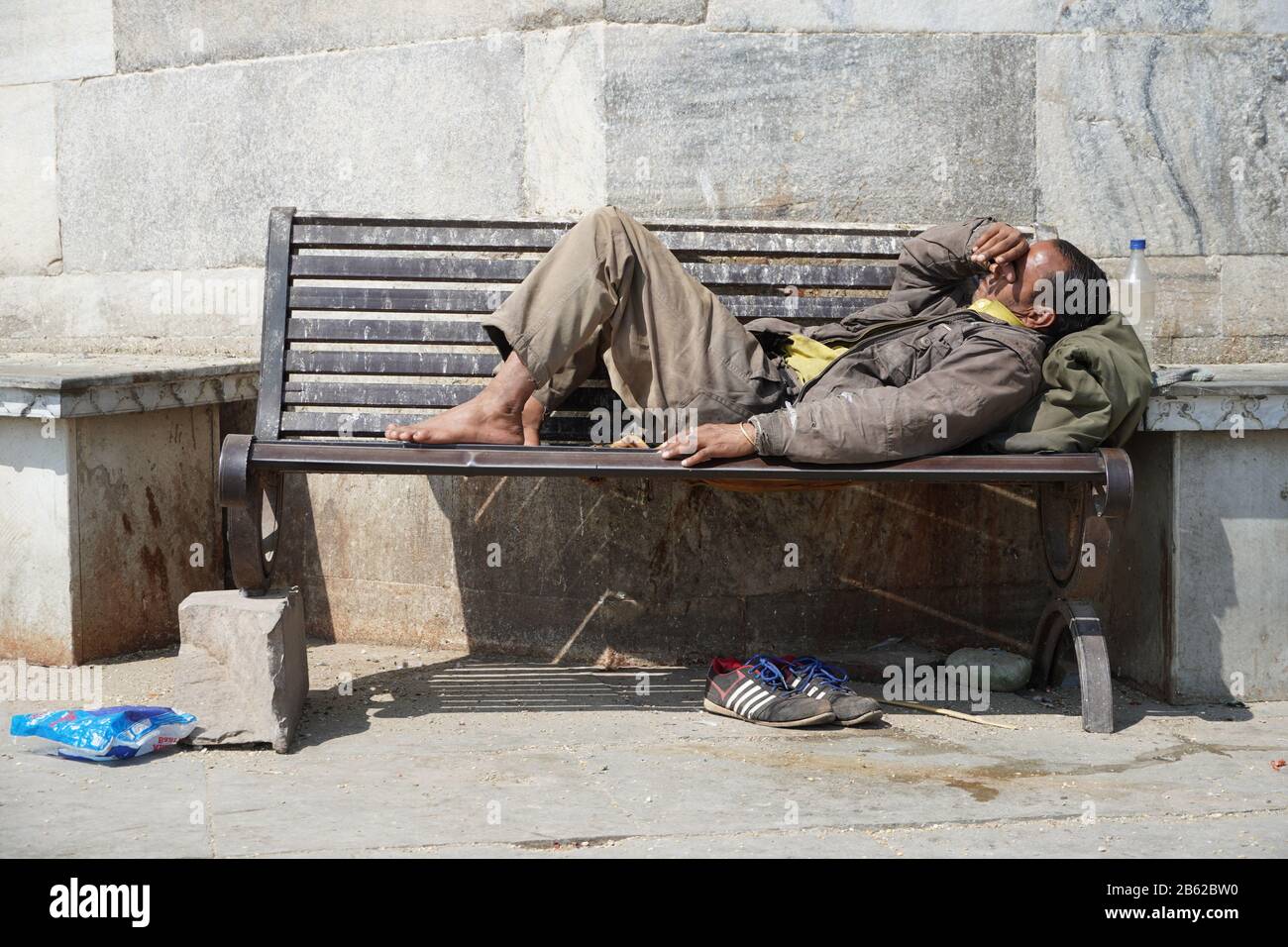 Poor homeless beggar man or refugee sleeping on a dirty wooden bench in ...