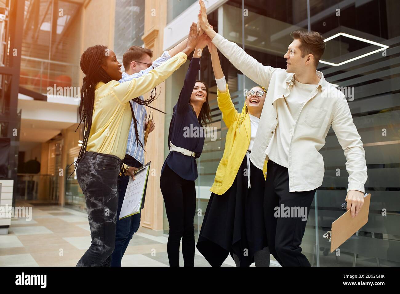 positive active young employees raising arms together, showing their ...