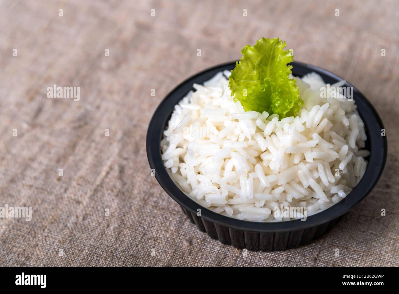 White boiled rice with leaf of green salad in black round bowl on a ...