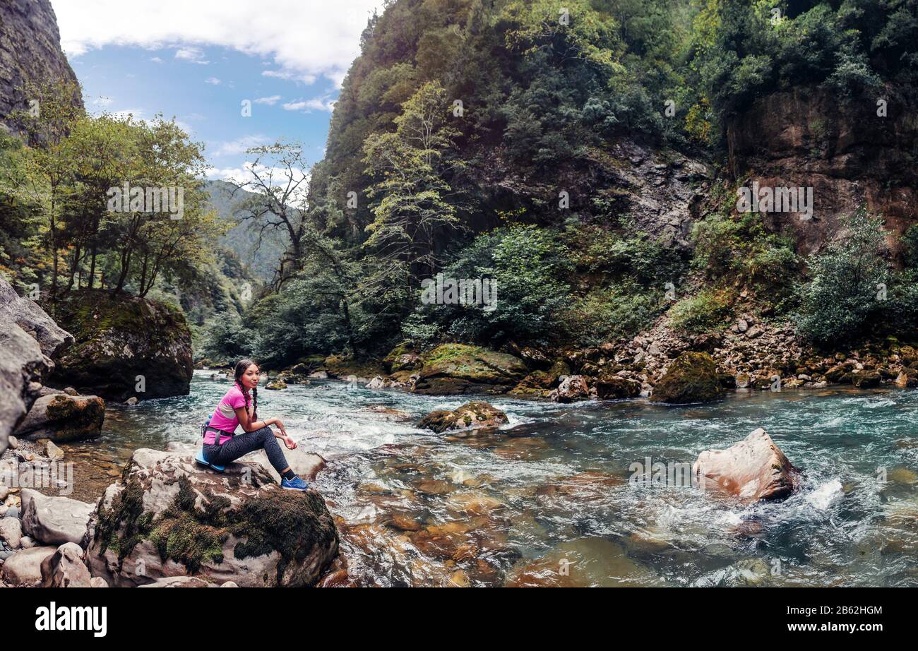 Cute Young Woman sitting on Stone on the shore of rapid mountains river ...