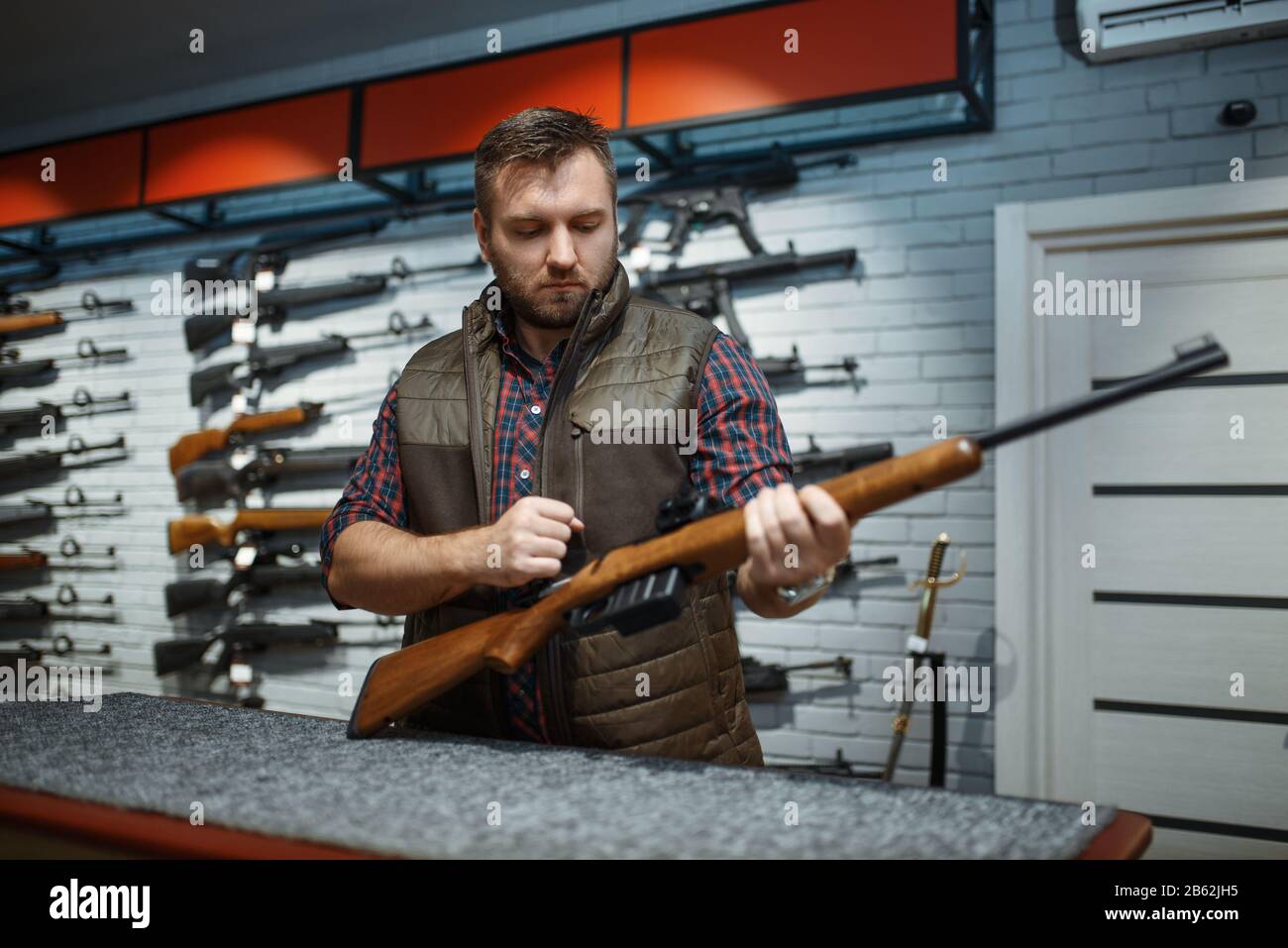 Man with rifle standing at counter in gun shop Stock Photo - Alamy