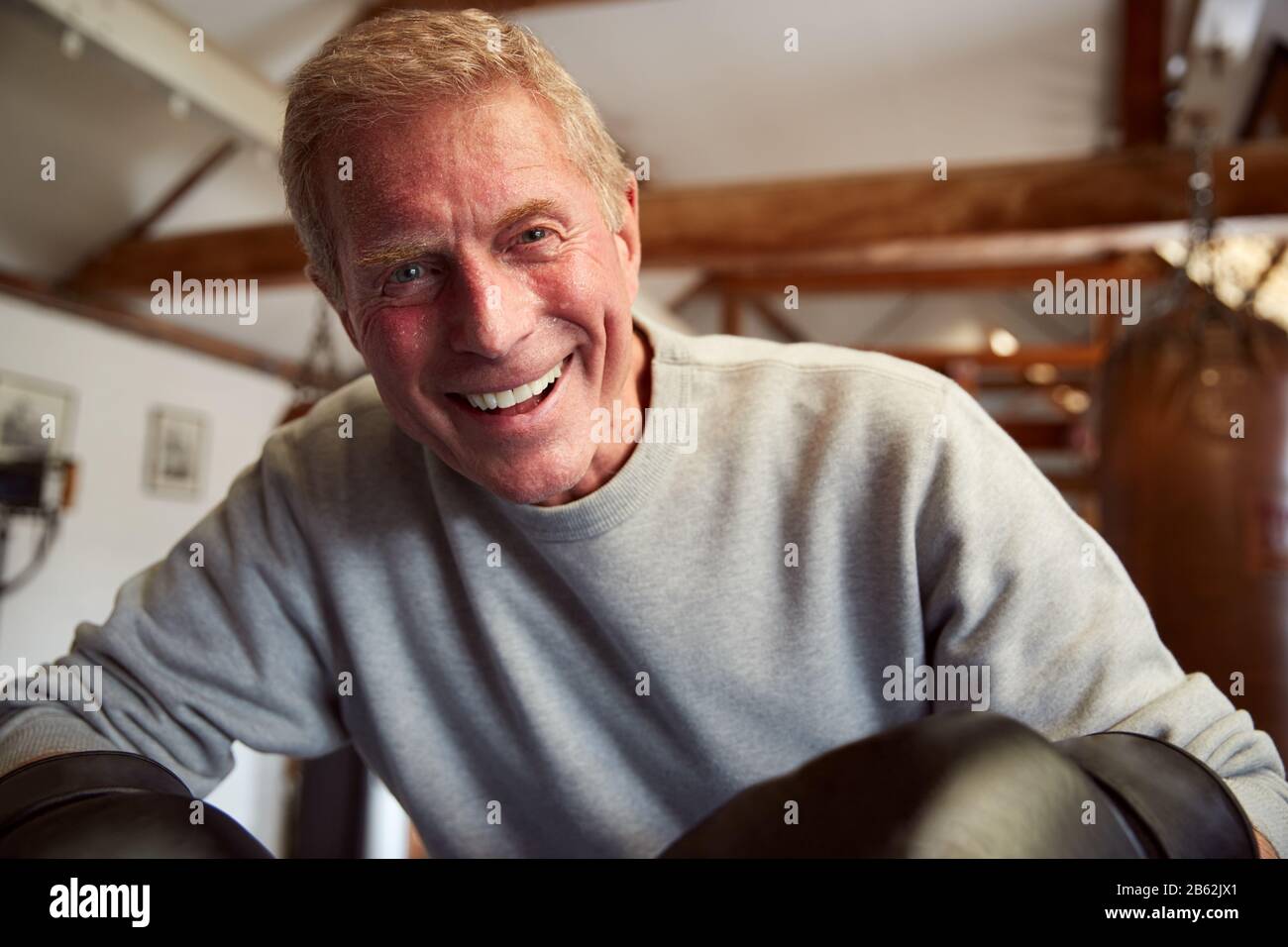 Smiling Senior Male Boxer In Gym Wearing Boxing Gloves Leaning On Ropes ...