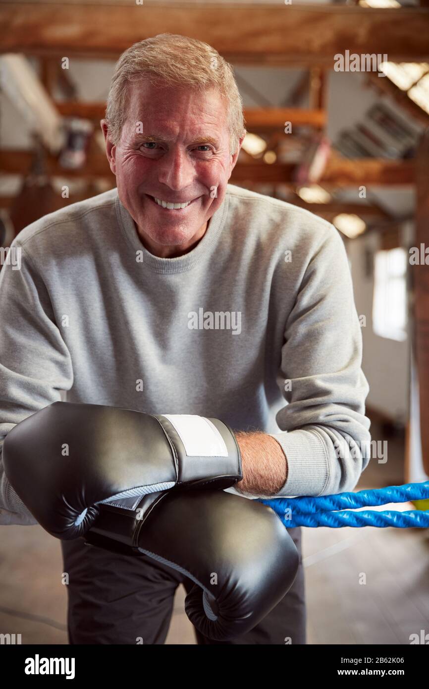 Smiling Senior Male Boxer In Gym Wearing Boxing Gloves Leaning On Ropes ...