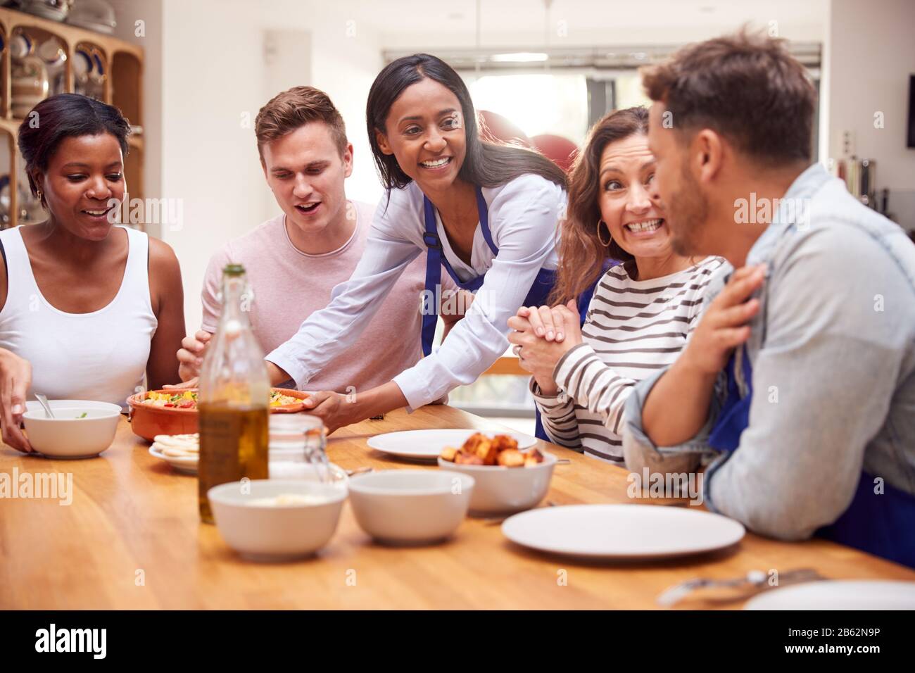 Group Of Friends Sitting Around Table Eating Meal At Home Together ...