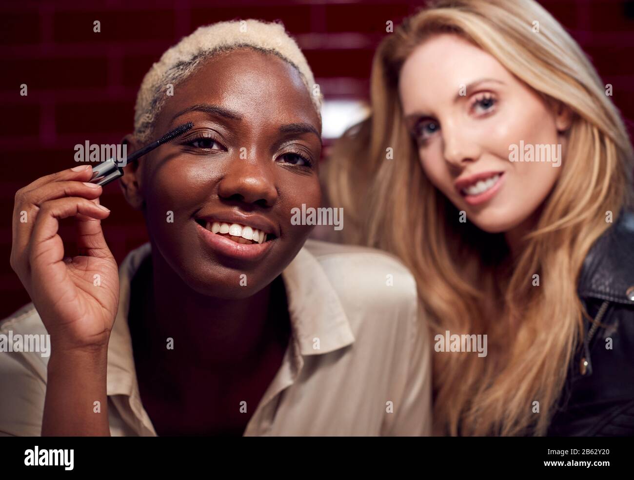 Two Young Female Friends Doing Make Up Reflected In Mirror Of Bathroom ...