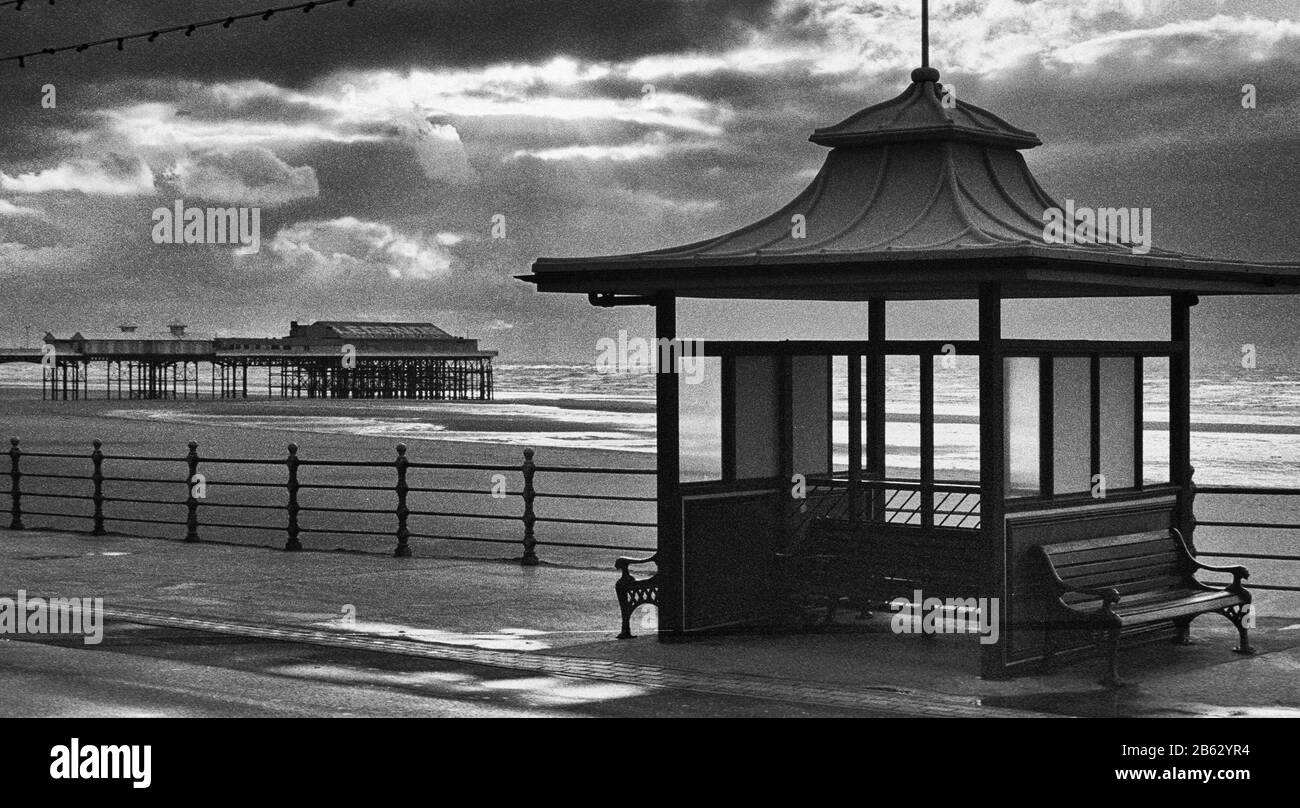 An empty shelter on the promenade with empty pier and beach behind, a ...