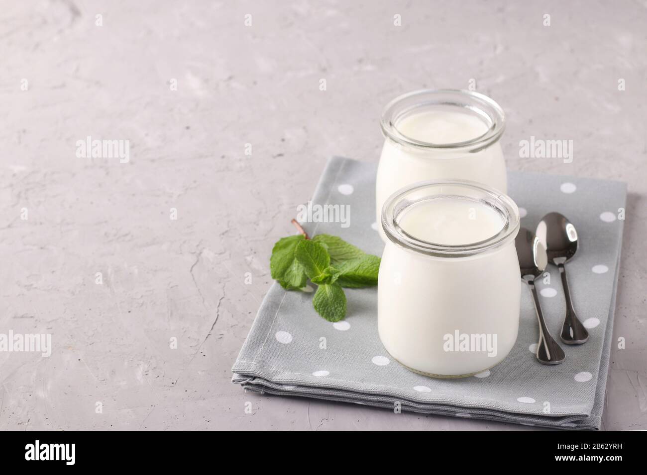 Two portions of homemade natural organic yogurt in glass jars on a grey ...