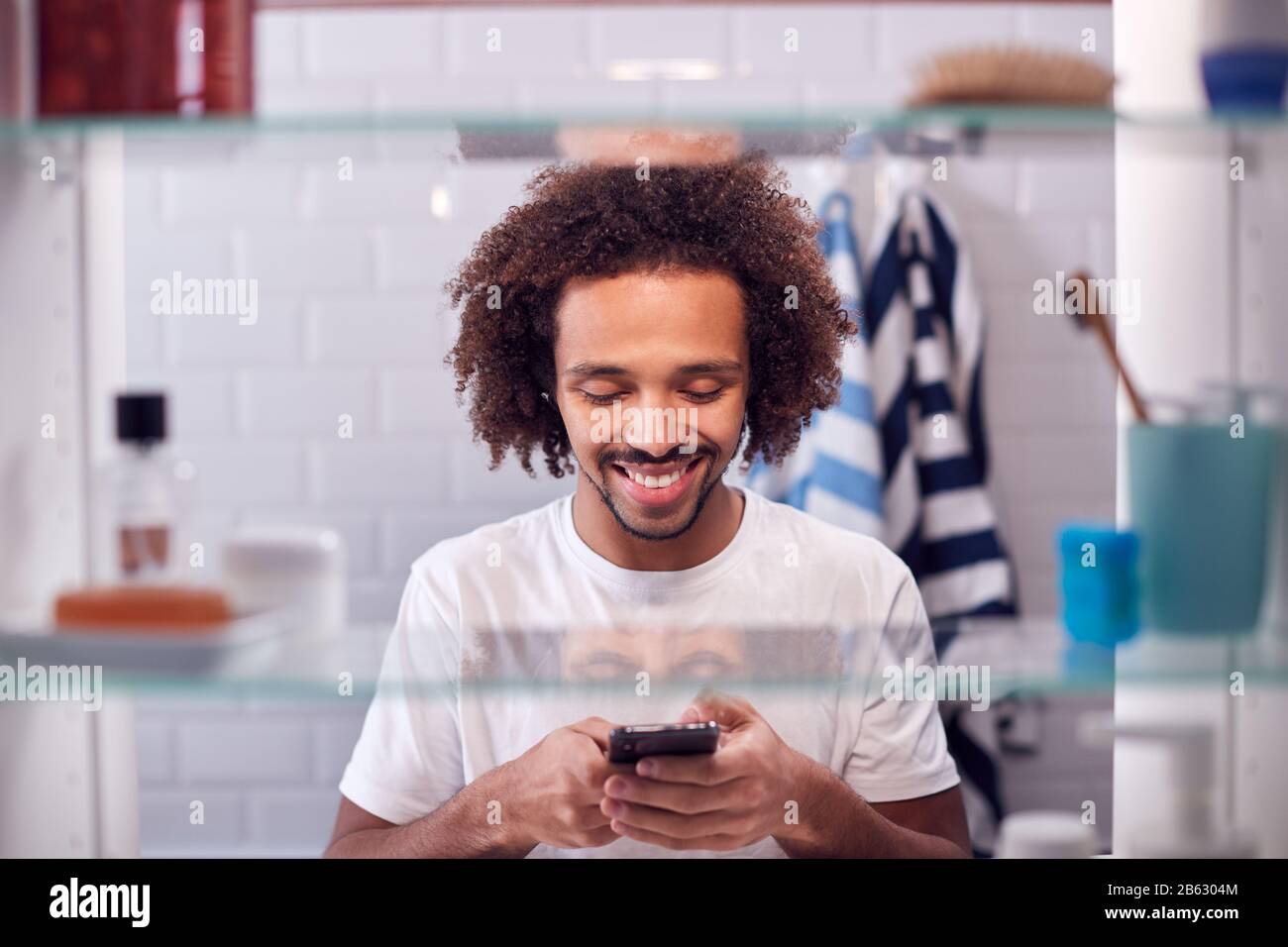 View Through Bathroom Cabinet Of Man Checking Messages On Phone Before ...
