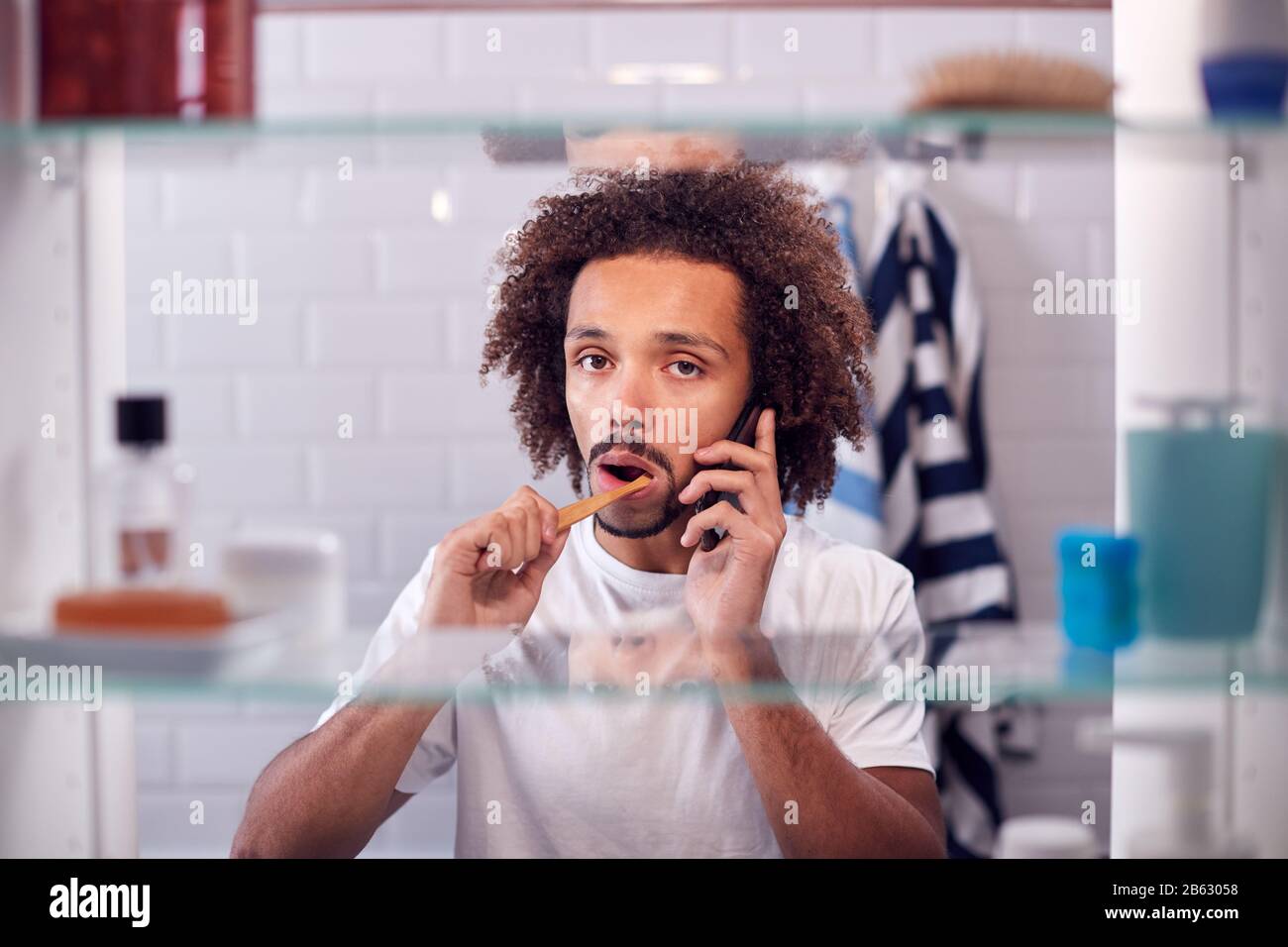 View Through Bathroom Cabinet Of Man Brushing Teeth And Talking On ...