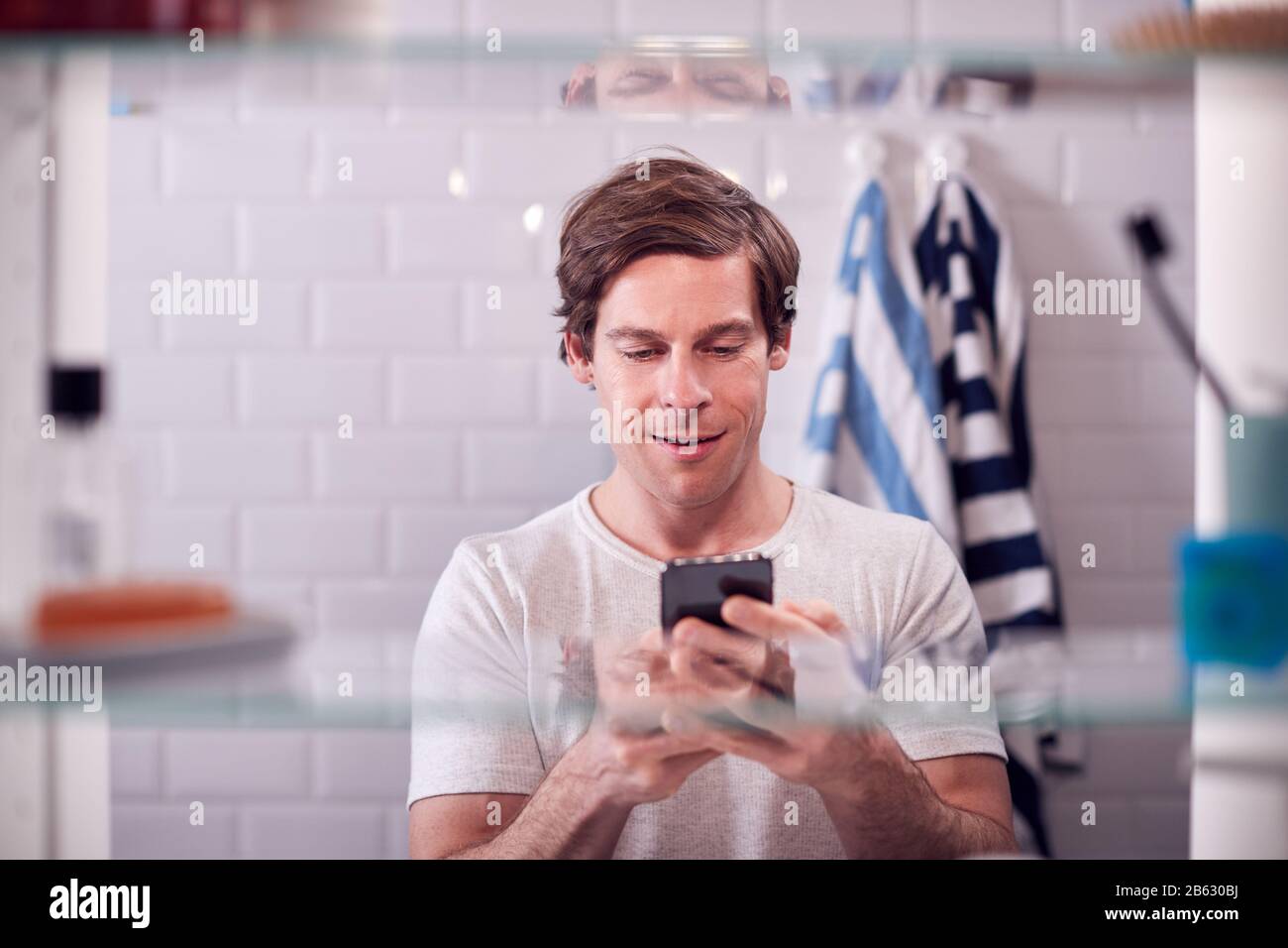View Through Bathroom Cabinet Of Man Checking Messages On Phone Before ...
