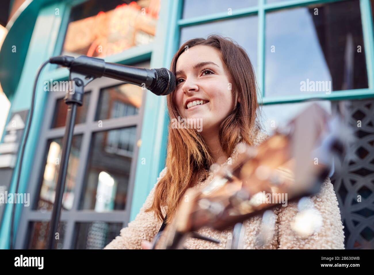 Female Musician Busking Playing Acoustic Guitar And Singing Outdoors In ...
