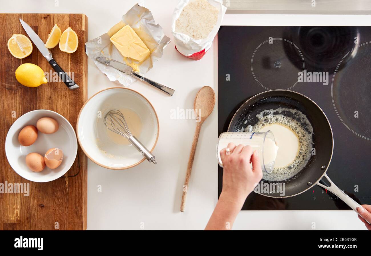 Overhead Shot Of Woman In Kitchen Pouring Batter Into Pan For Pancakes ...