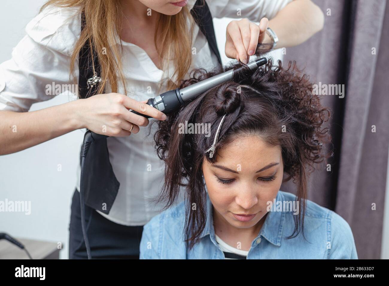 Young cheerful girl doing hairstyle in a barbershop. The girl smiles ...