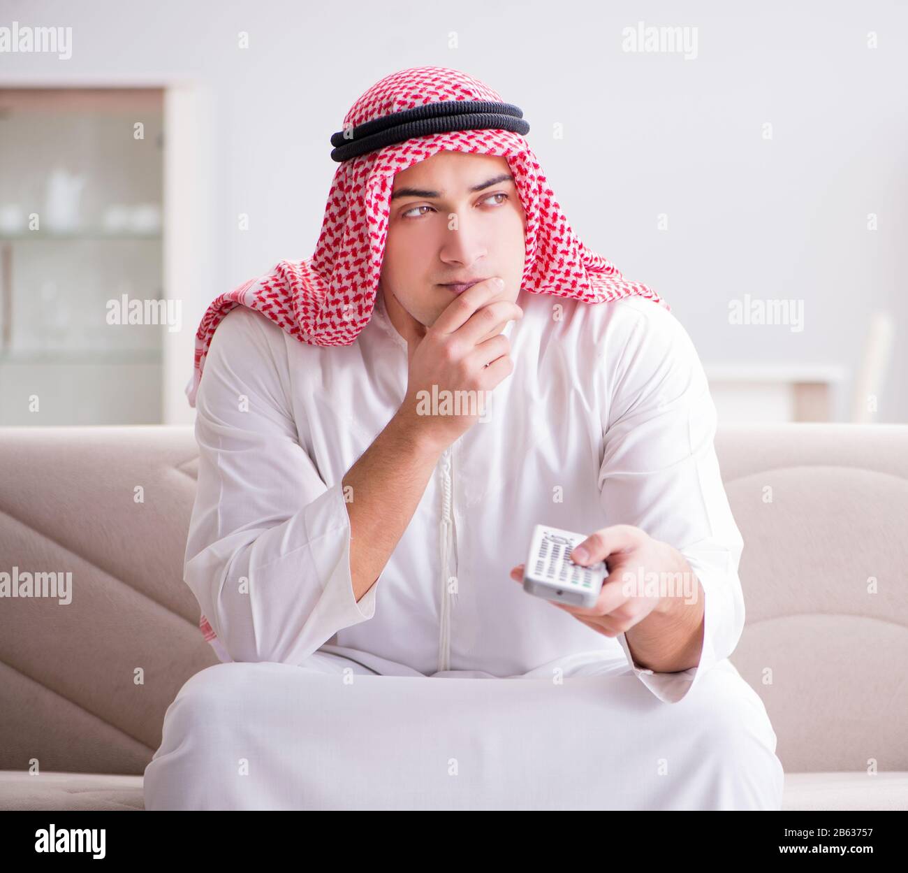 The young arab man watching tv sitting on the sofa Stock Photo - Alamy