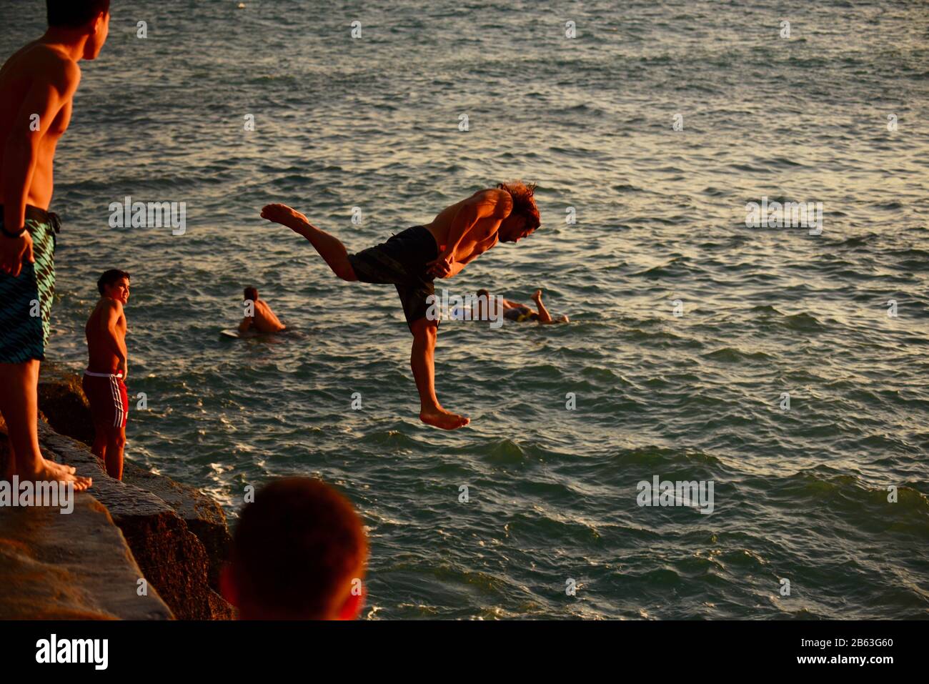 Cliff jumpers, wearing board shorts, jumping off ledge into ocean at ...