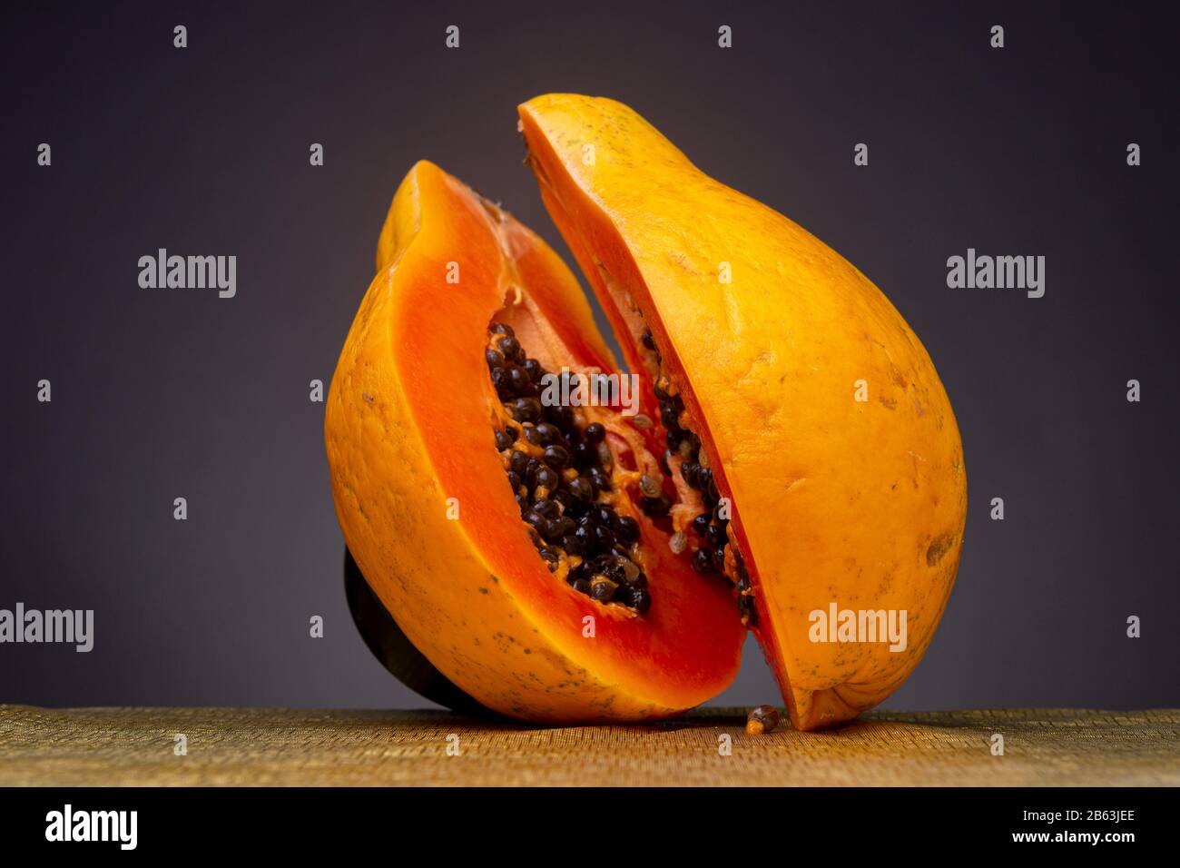 Bright vibrant orange papaya fruit sliced and half opened up on a gold ...