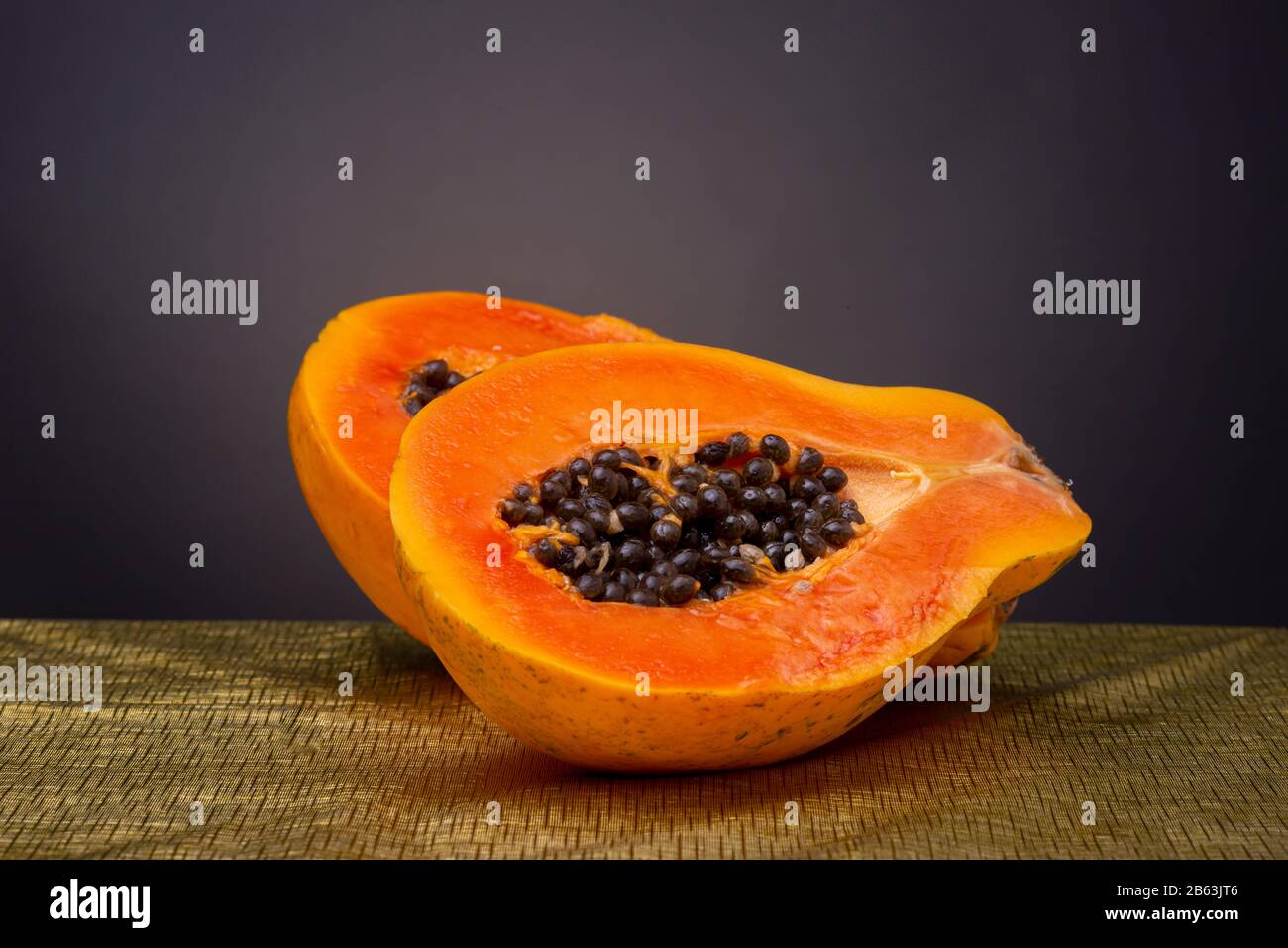 Bright vibrant orange papaya fruit sliced in half on a gold coloured ...