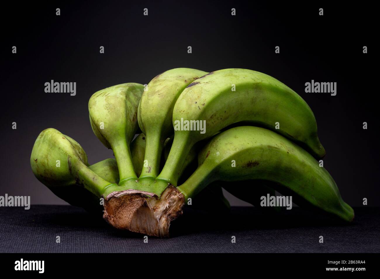 Brightly lit vibrant green banana laying on a black surface with dark ...