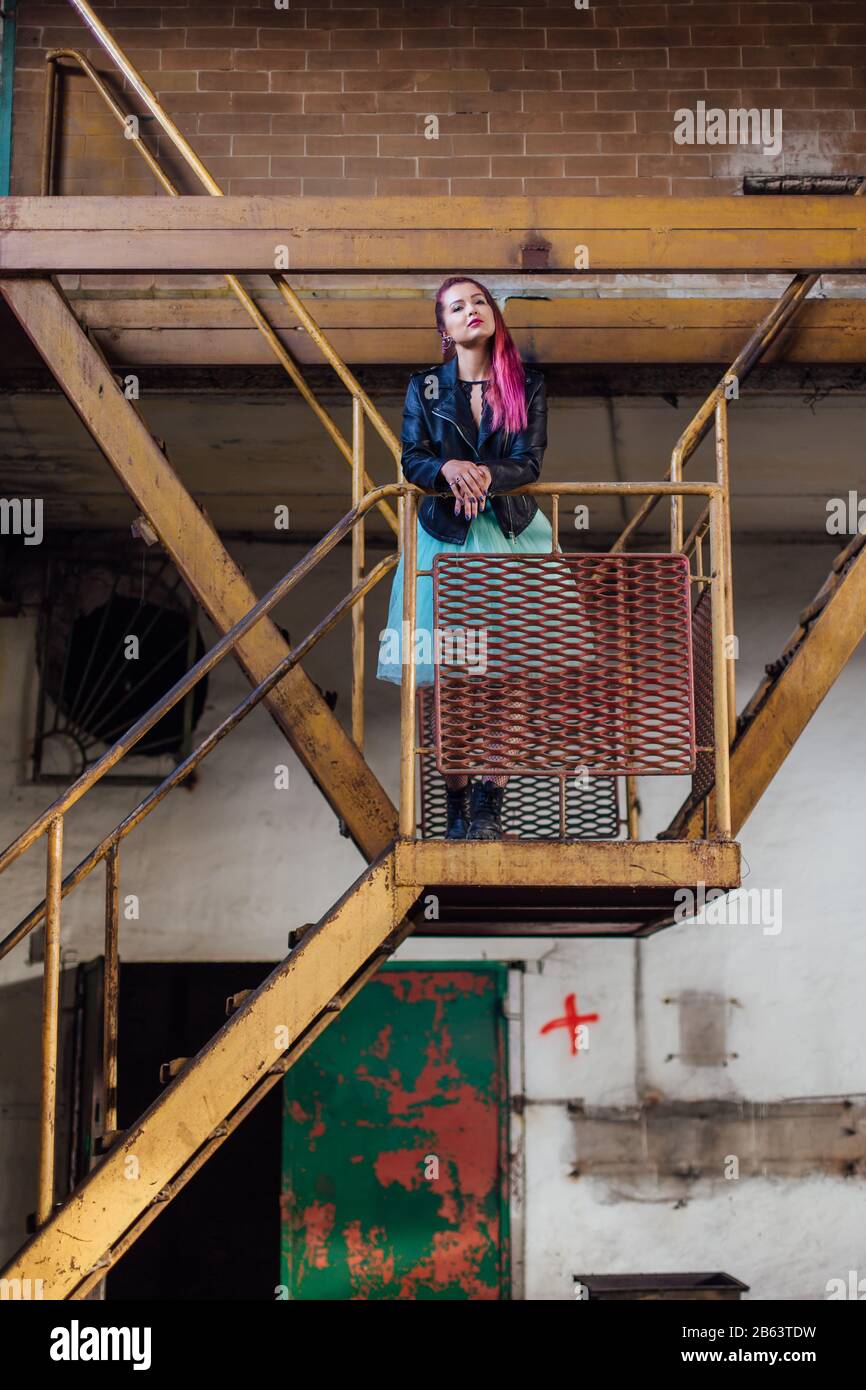 Portrait of a young girl with pink hair standing on the rusty stairs ...