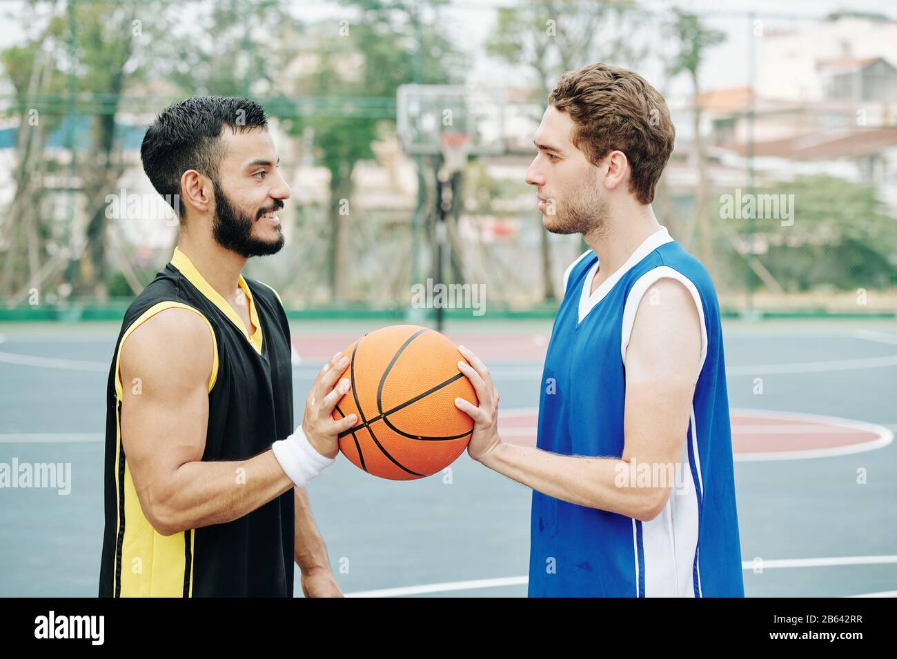 Smiling basketball players from different teams holding ball and ...