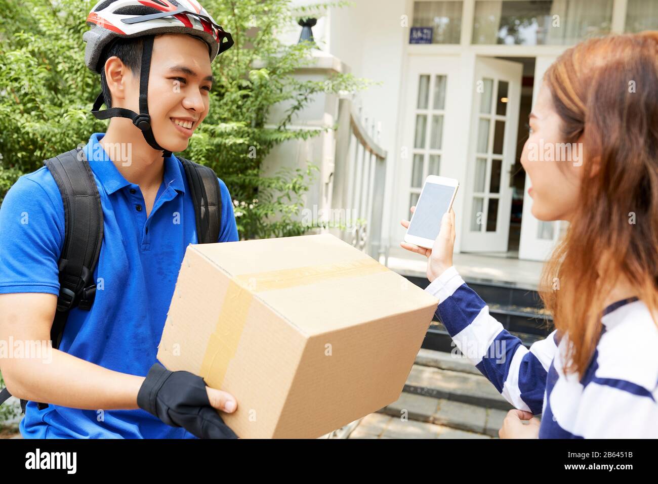 Young woman telling delivery man that she is paying for shipping with ...