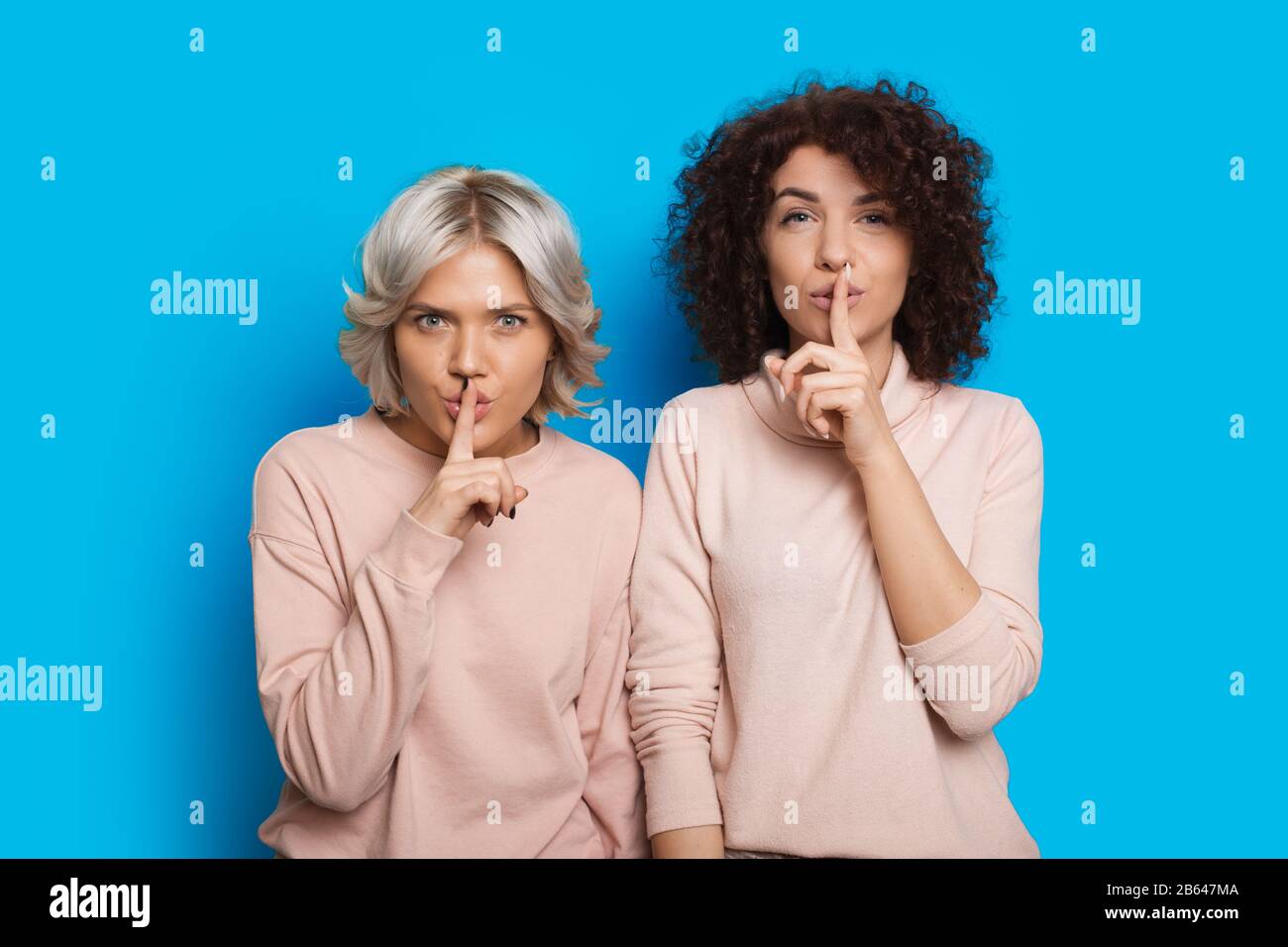 Two curly haired caucasian girls are gesturing the silence sign while ...