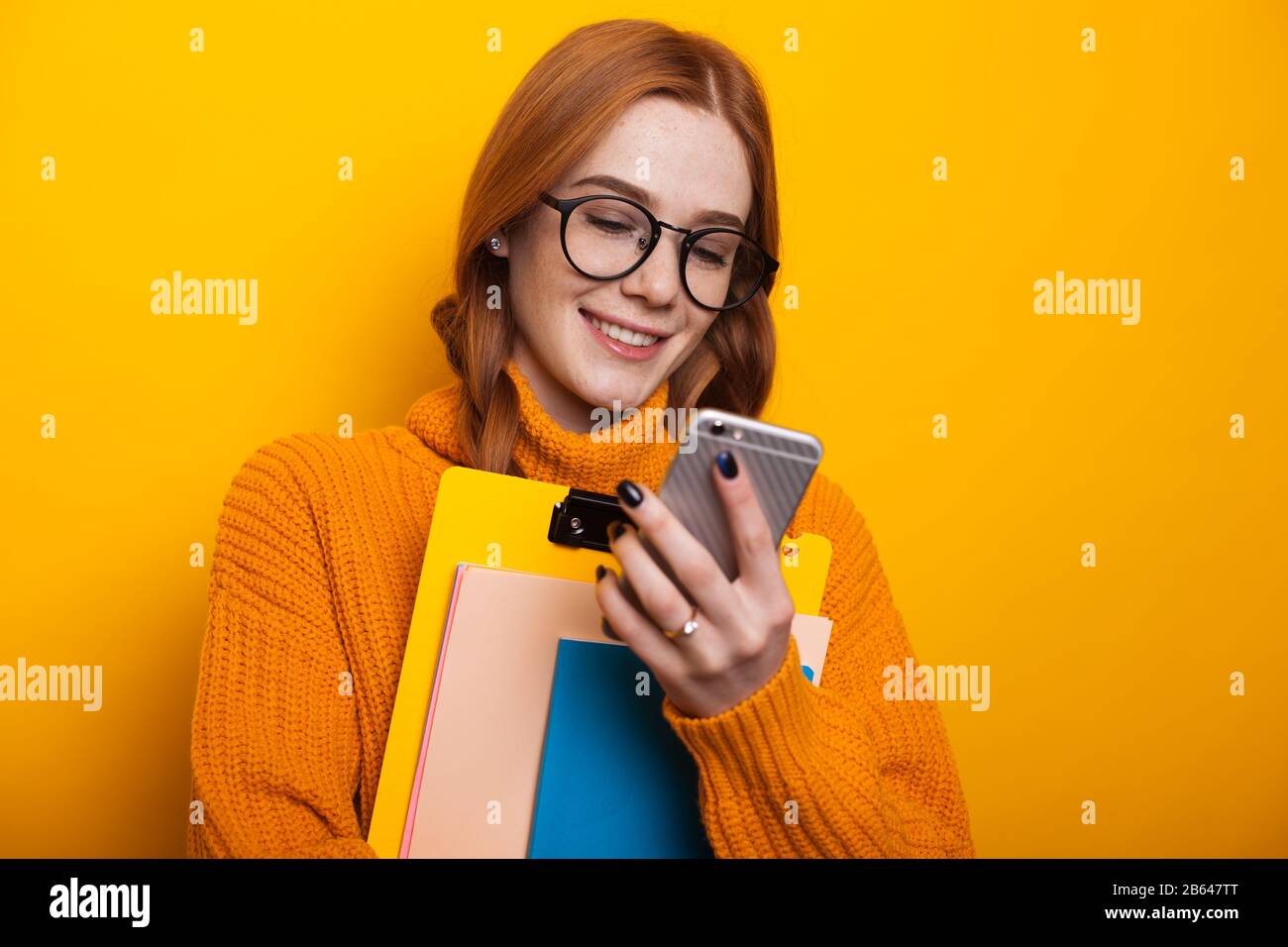 Charming caucasian student holding some books and chatting on phone ...