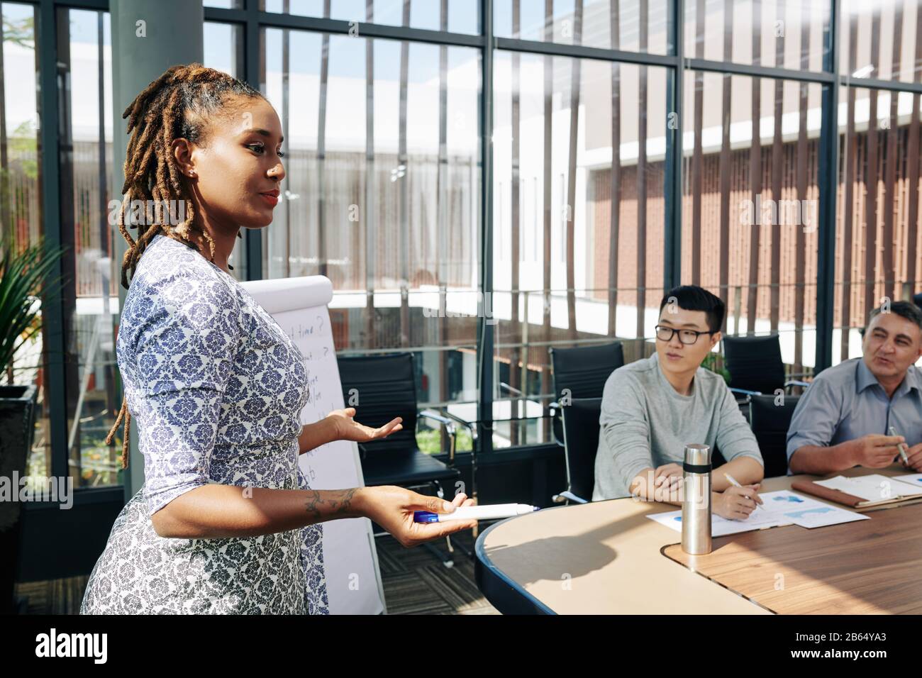 Pretty Hispanic businesswoman talking in front of colleagues in meeting ...