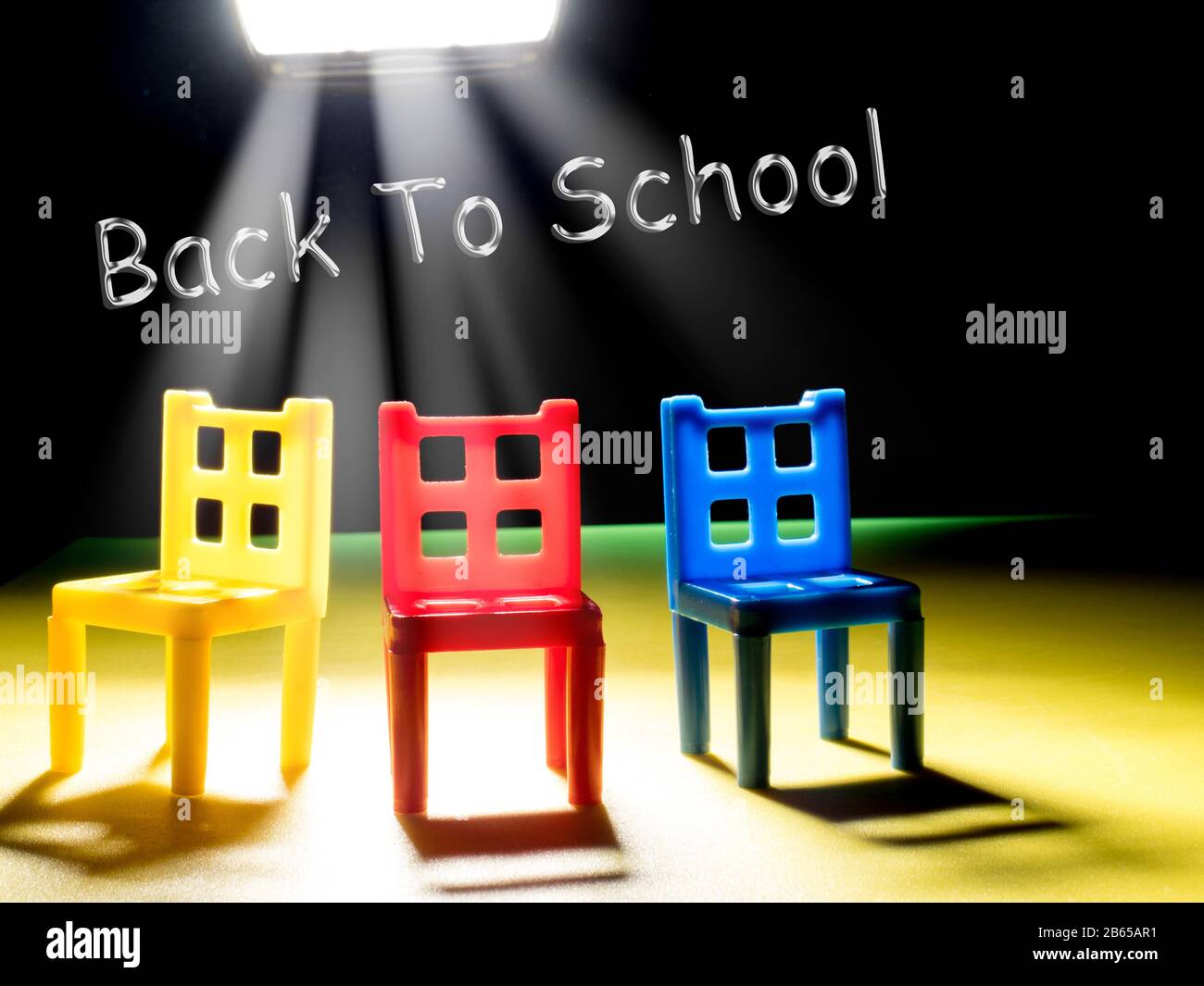 Three empty colorful school chairs are back lit by a bright white ...