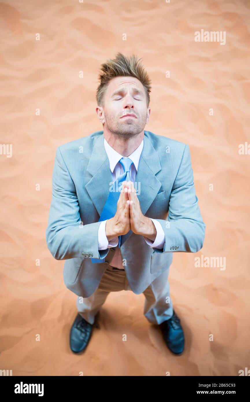 Stranded businessman looking up for help standing on red sand desert ...