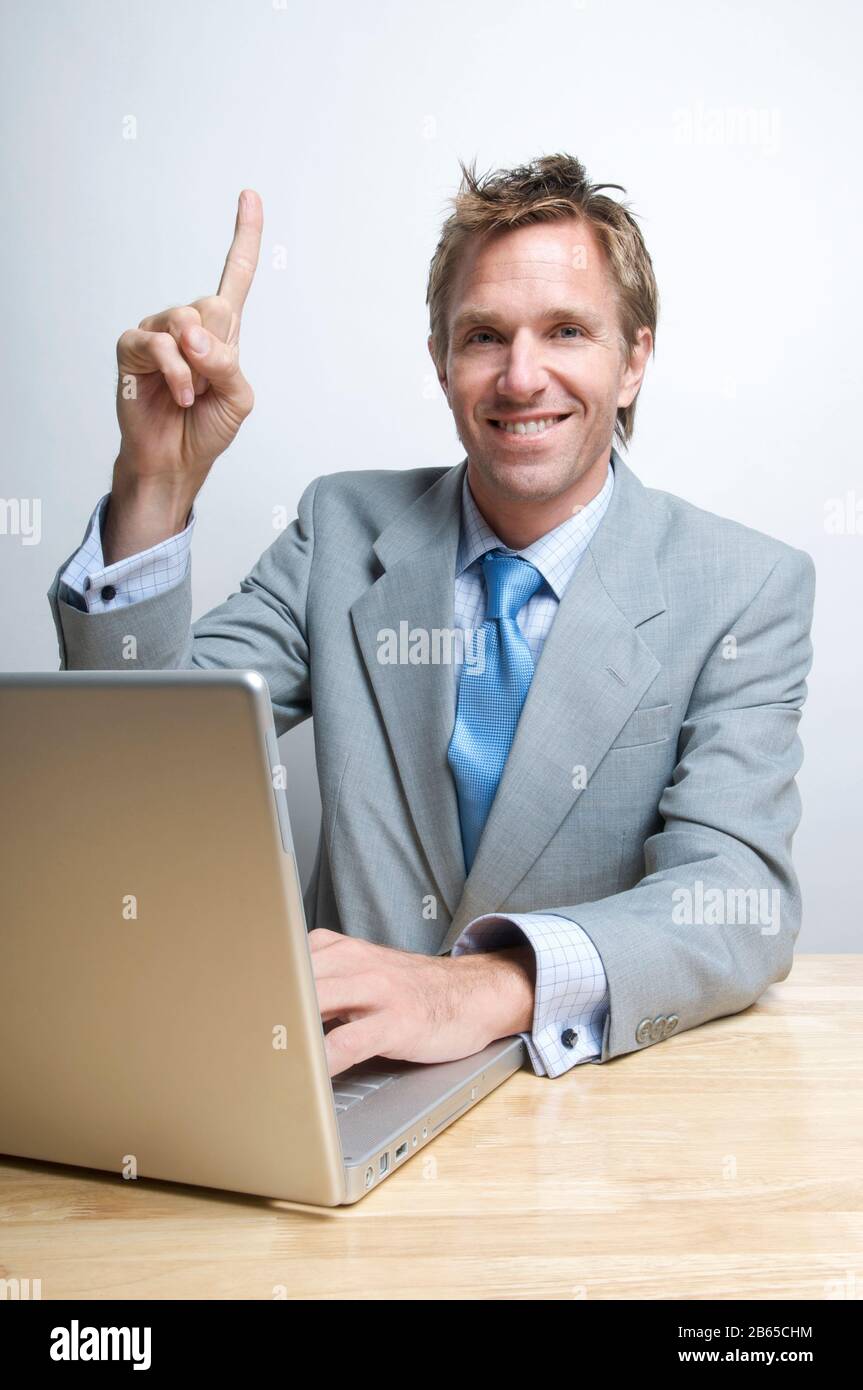 Smiling businessman sitting in front of his laptop computer raising a ...