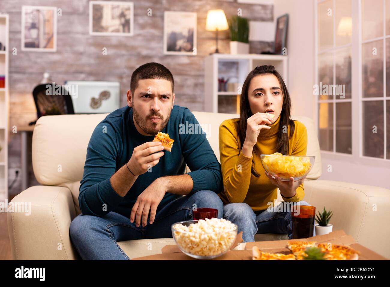 Beautiful young couple watching TV and eating fast food takeaway in the ...