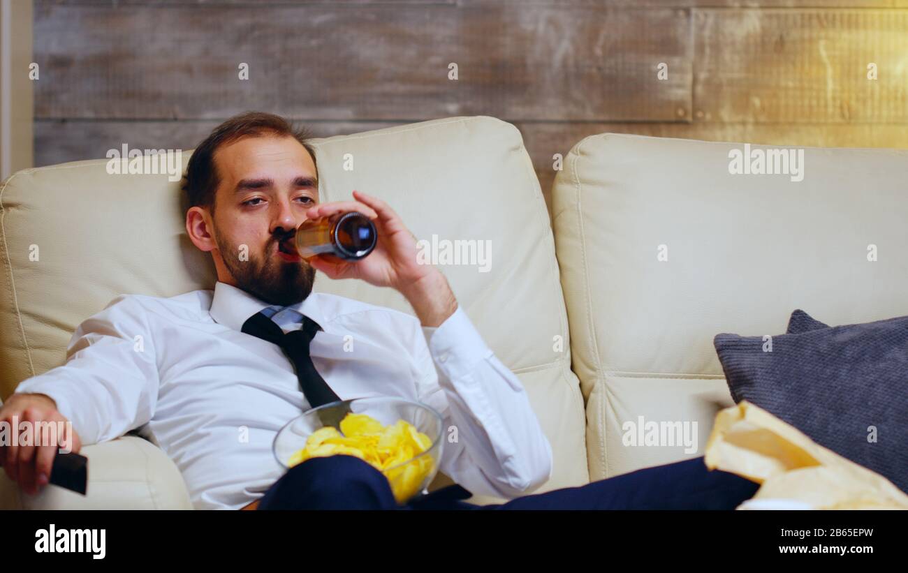 Overworked businessman sitting on couch using tv remote control and ...