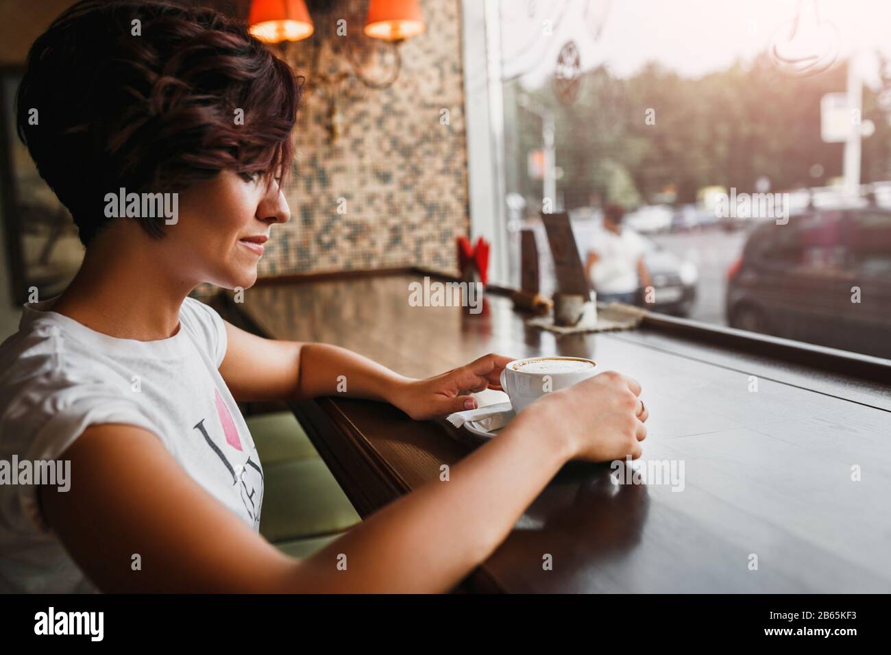 Woman in vintage cafe sitting and drinking coffee by the window looking ...