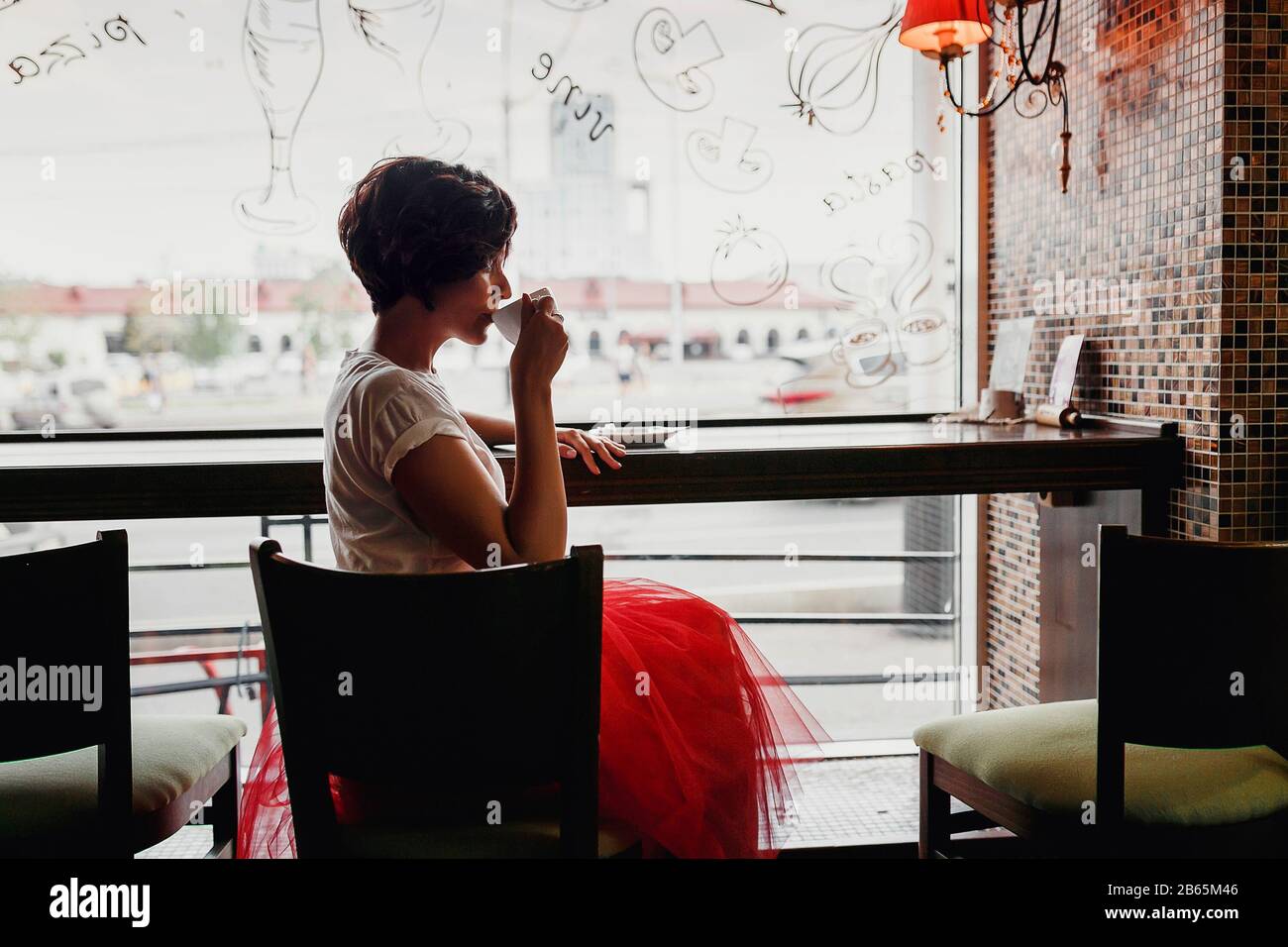 Woman in vintage cafe sitting and drinking coffee by the window looking ...