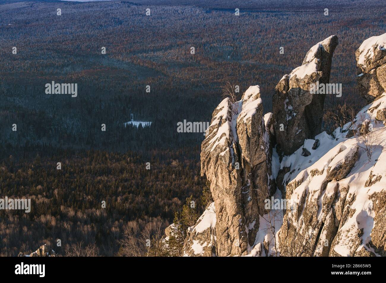 Rocky peak of basalt pillars covered by snow, winter forest in the ...