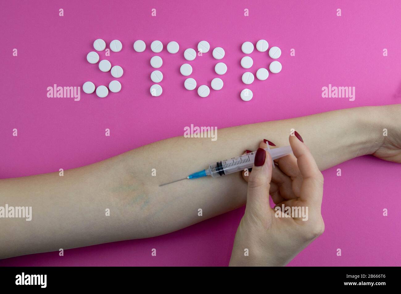 The word stop is laid out of tablets and a hand with a syringe which ...