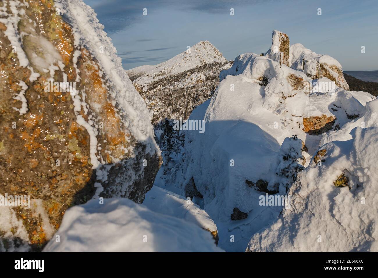 Rocky peak of basalt pillars covered by snow, winter forest in the ...