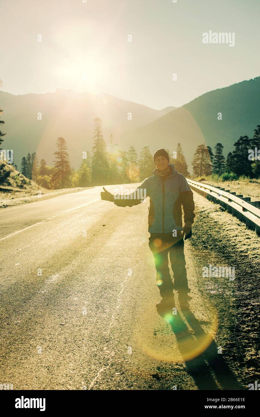 Man On Vacation Hitchhiking Along Country Road in mountains. Sun Flare ...