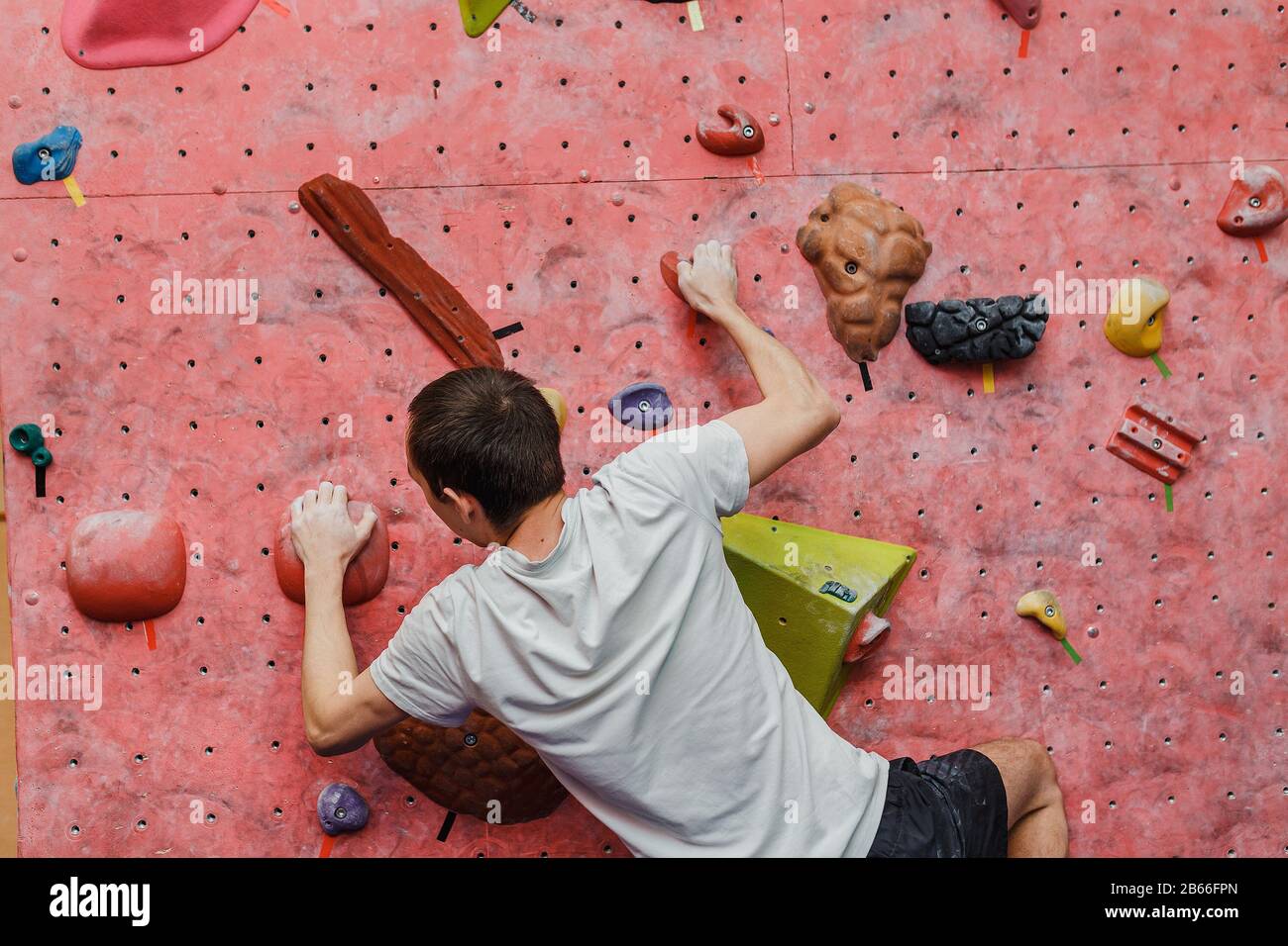 Free climber young man climbing artificial boulder indoors, back view ...