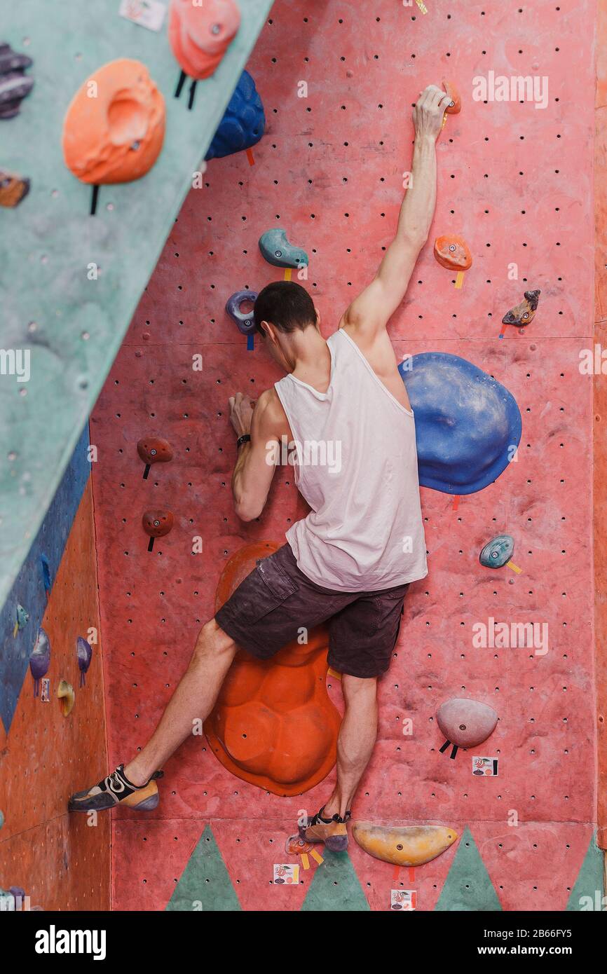 Free climber young man climbing artificial boulder indoors, back view ...