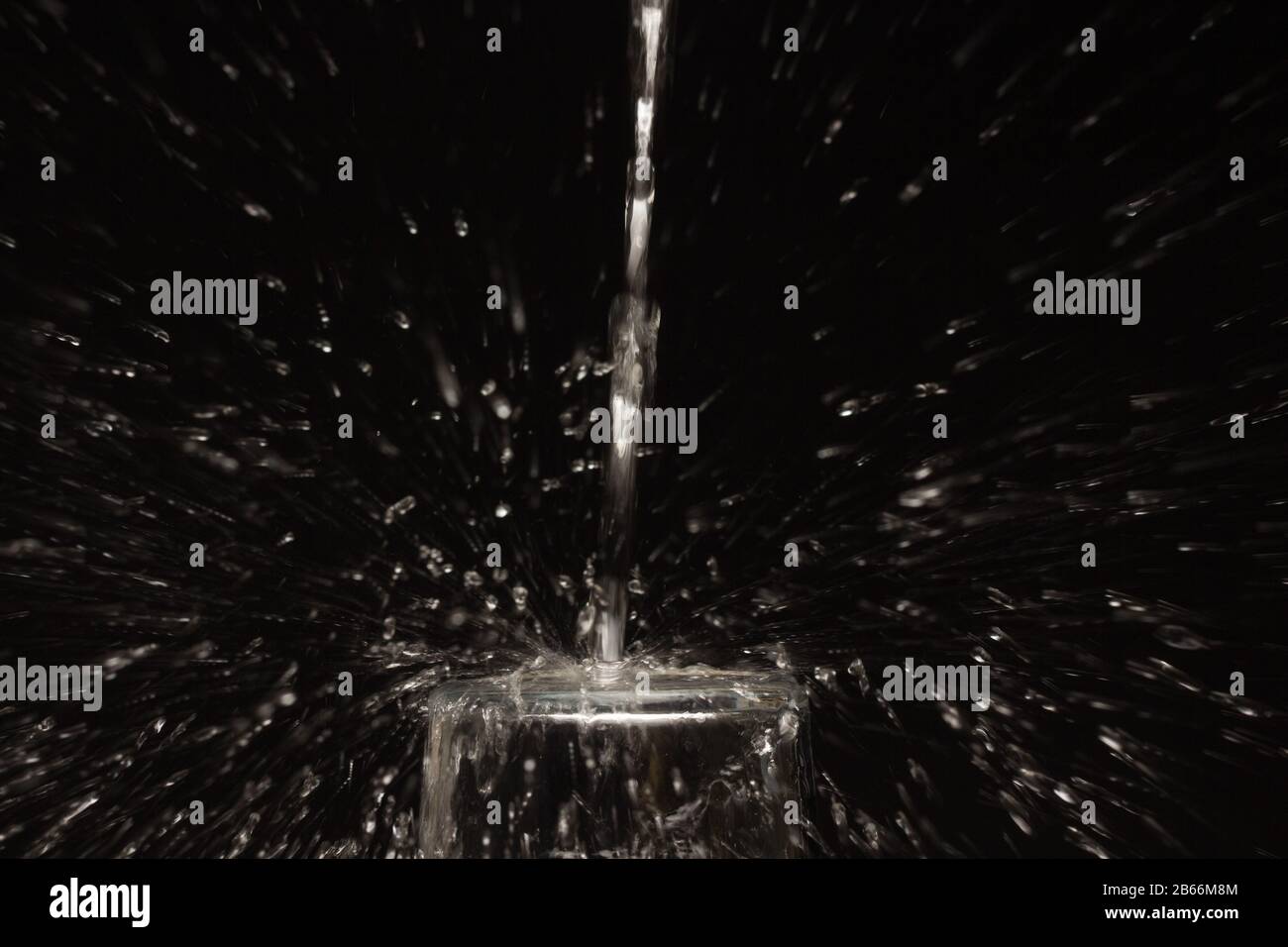 Water jet falling into a glass and generating a splash of water ...