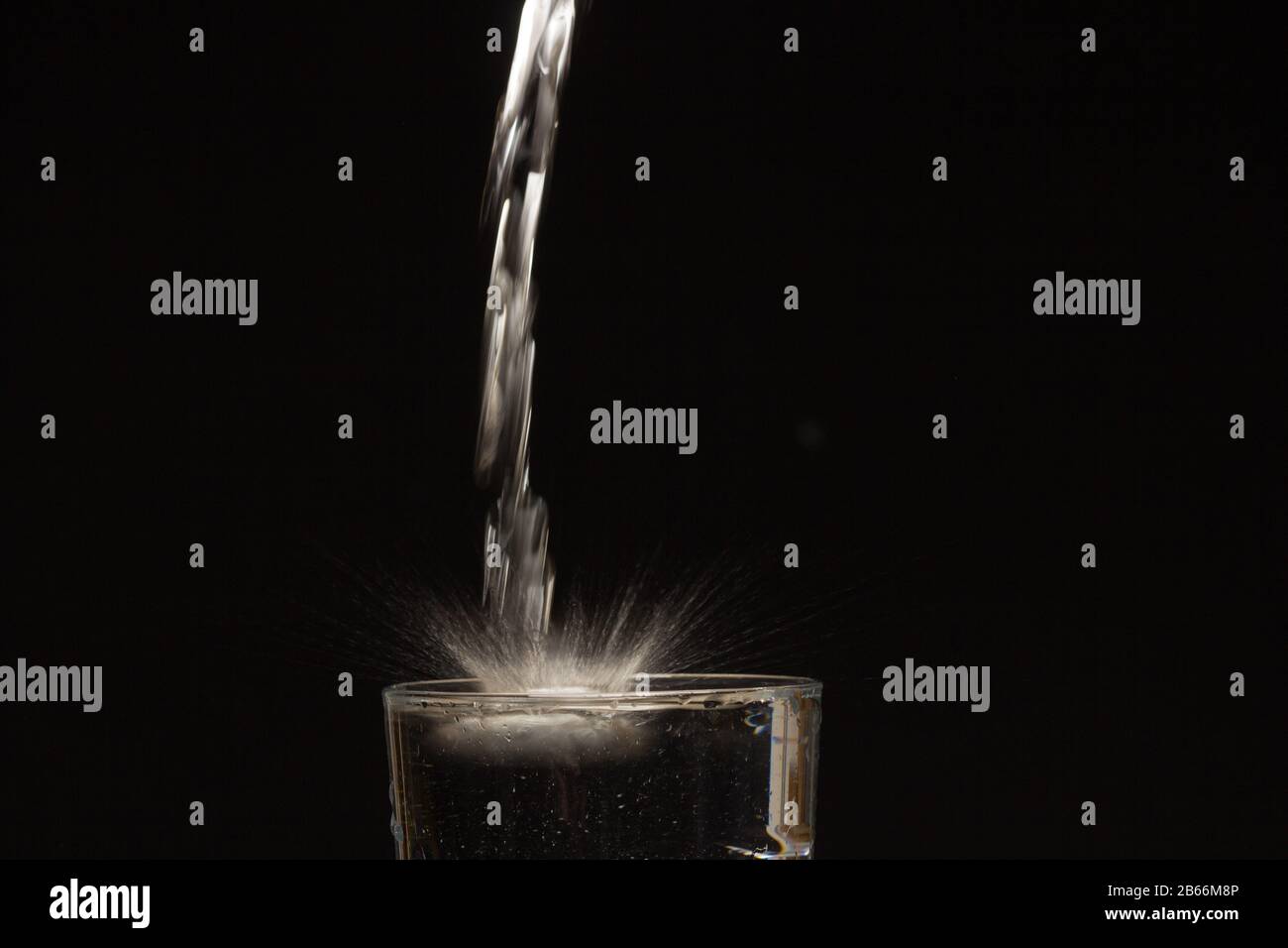 Water jet falling into a glass and generating a splash of water ...