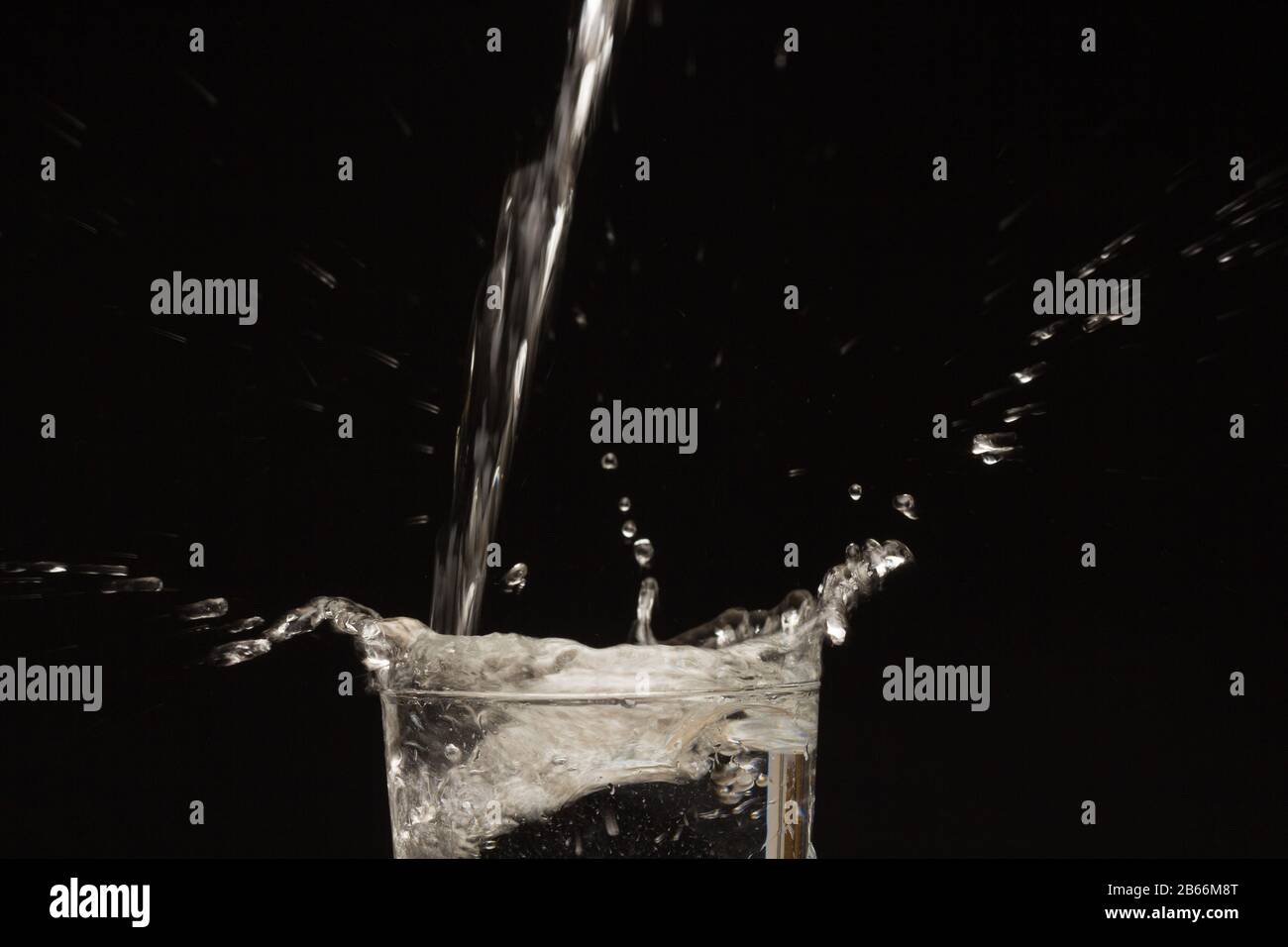 Water jet falling into a glass and generating a splash of water ...