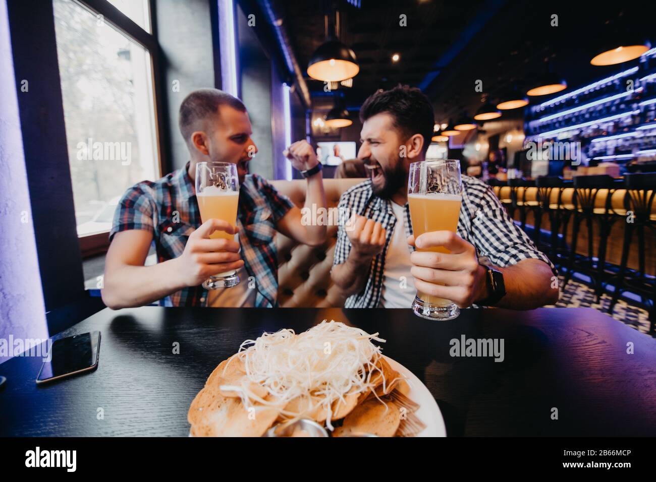 Two cheerful excited young men watching match on laptop and supporting ...