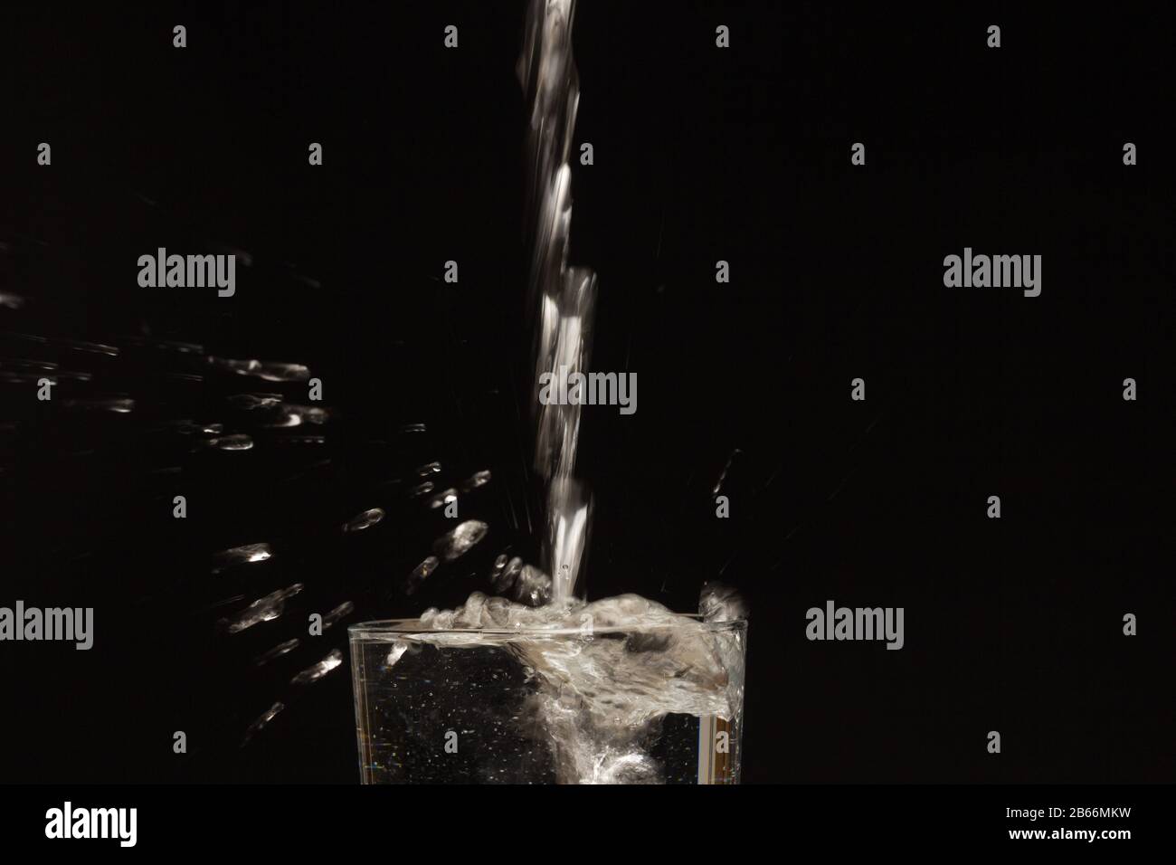 Water jet falling into a glass and generating a splash of water ...