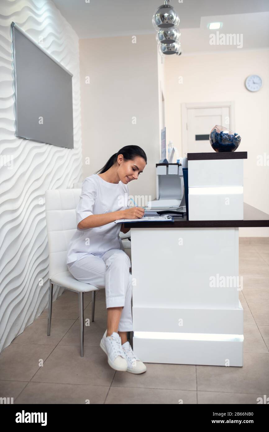 Receptionist wearing white uniform and sneakers making notes Stock ...