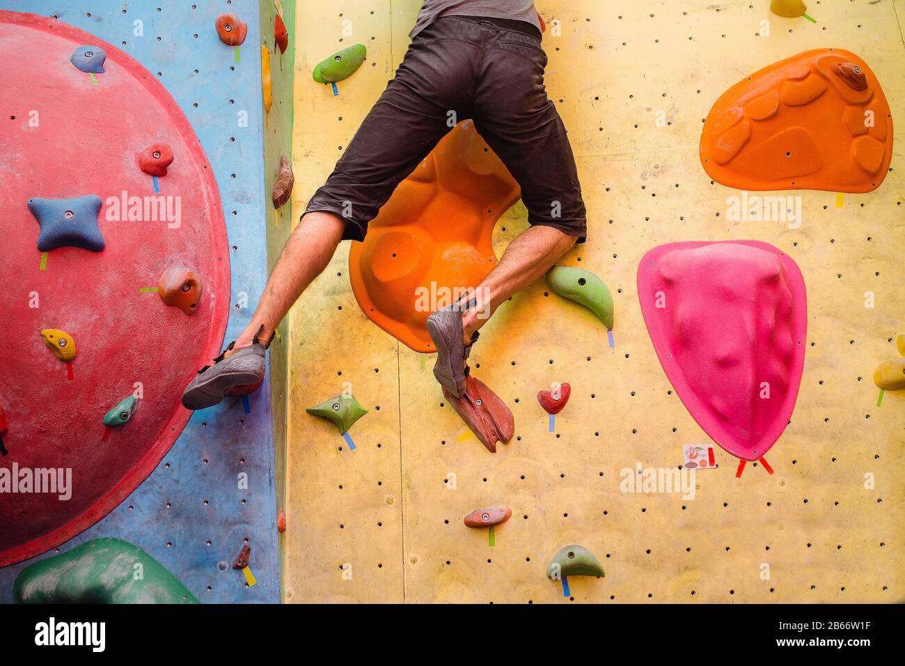 male climber training in bouldering gym wall, close up of leg muscles ...