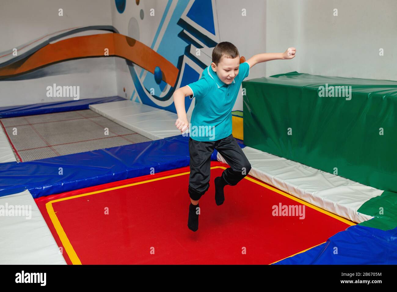 Boy is jumping high in striped tights on the big trampoline in kid ...
